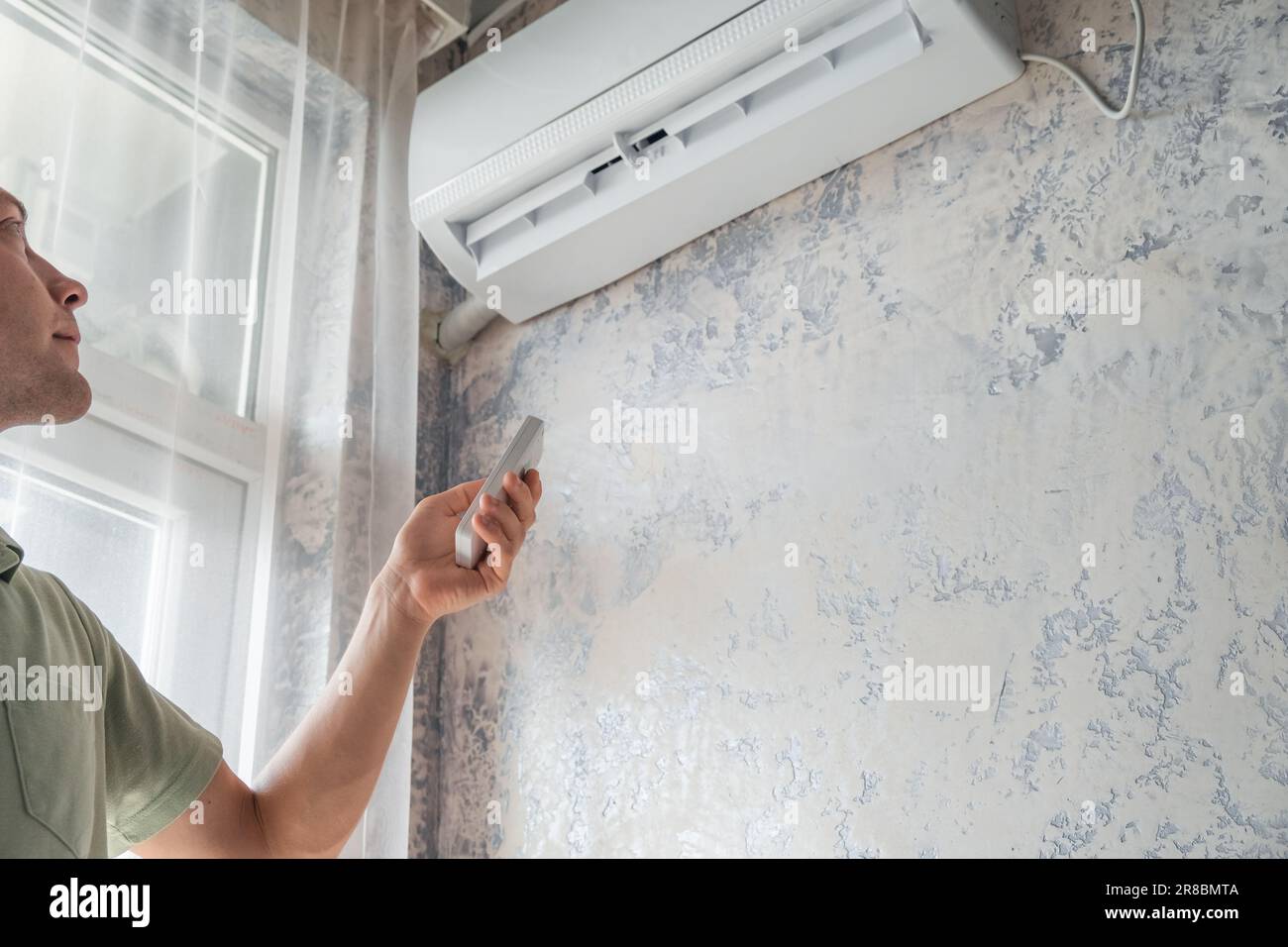 Young woman switching on air conditioner at home for comfort temperature with remote controller ...