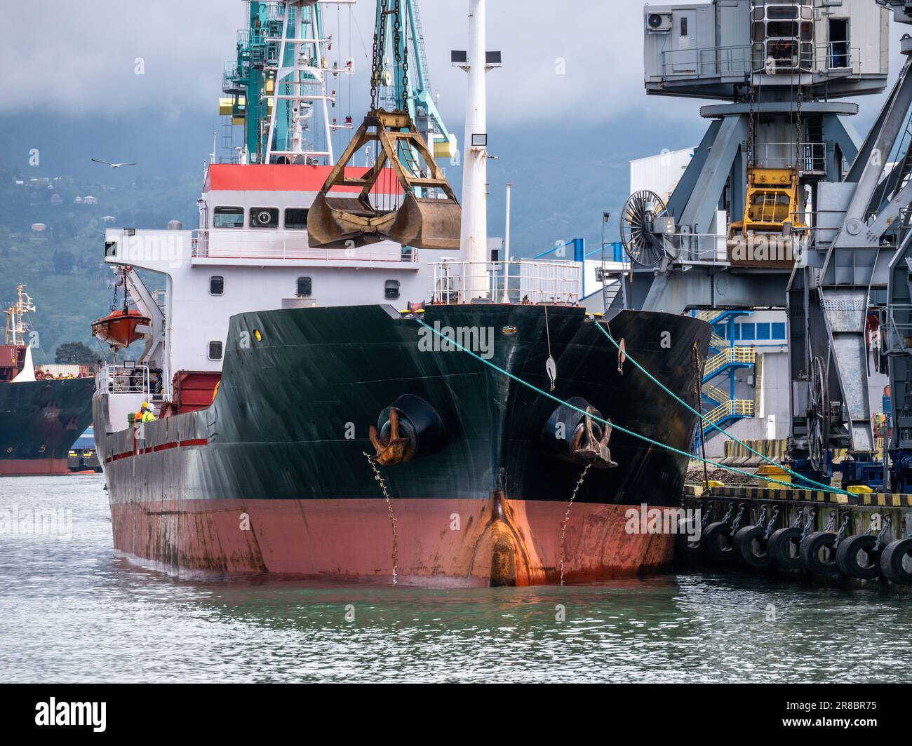 Cargo freight ship loading by bucket crane in industrial harbor or port ...