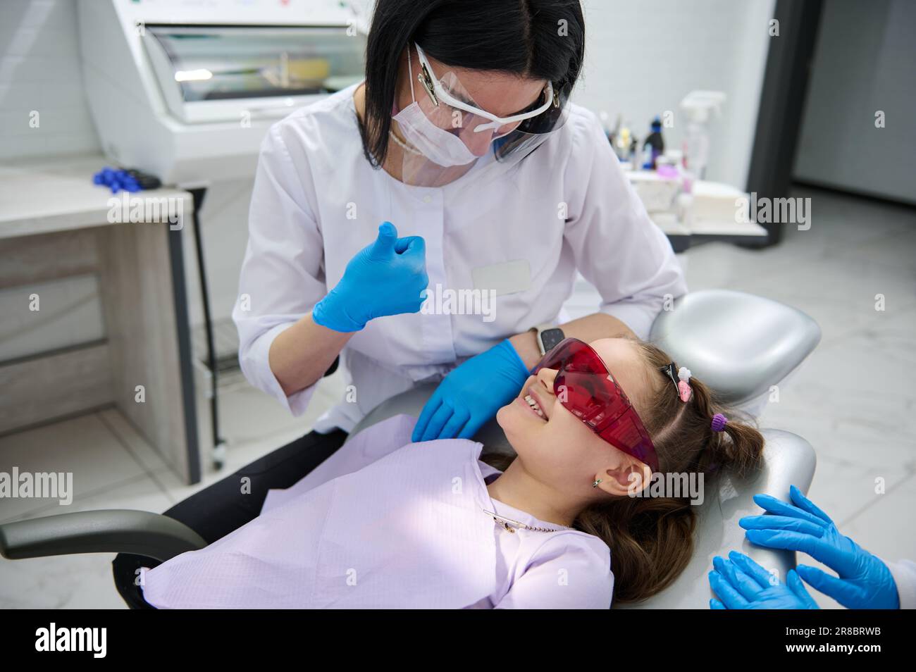 Adorable little girl with open mouth, being examined by a dental hygienist, orthodontist in ...