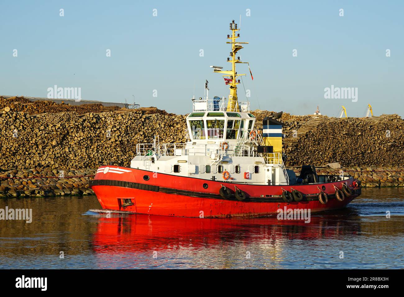 Powerful tugboat with a red hull sailing in harbor channel on wooden ...