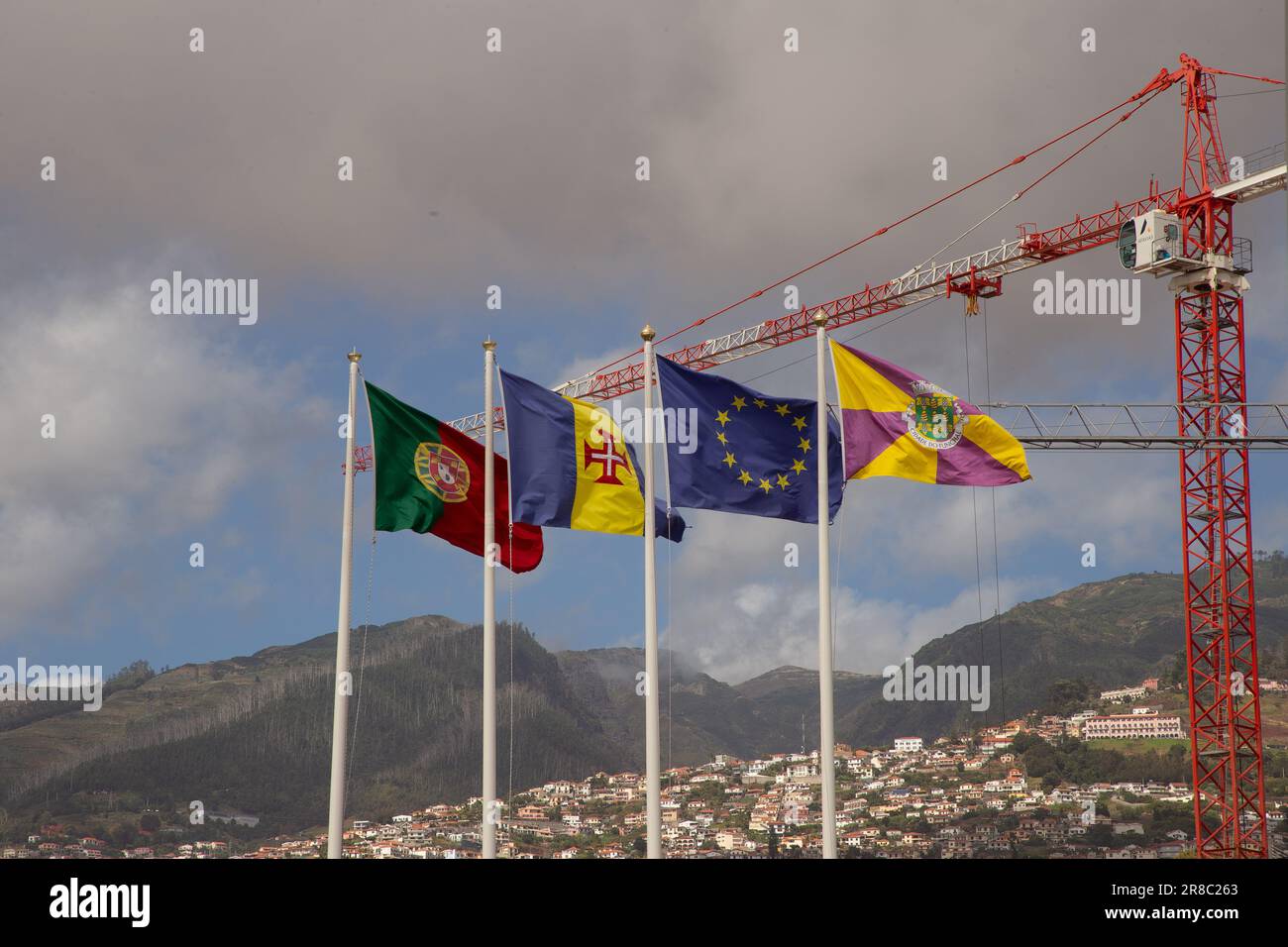 flags flying by a construction cranes against a madeira mountain ...