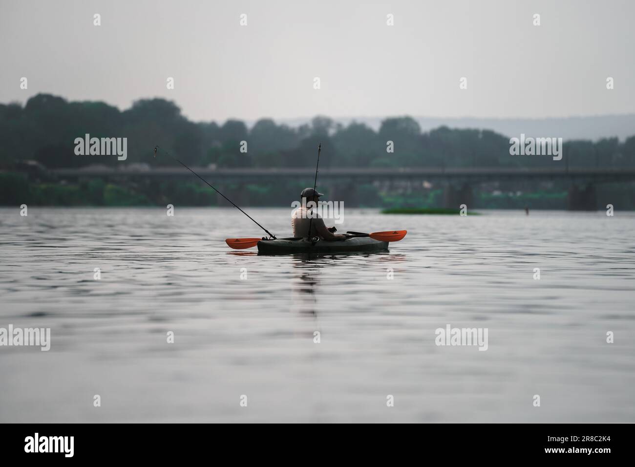 Man sitting in a green kayak with orange paddles facing away in a river ...