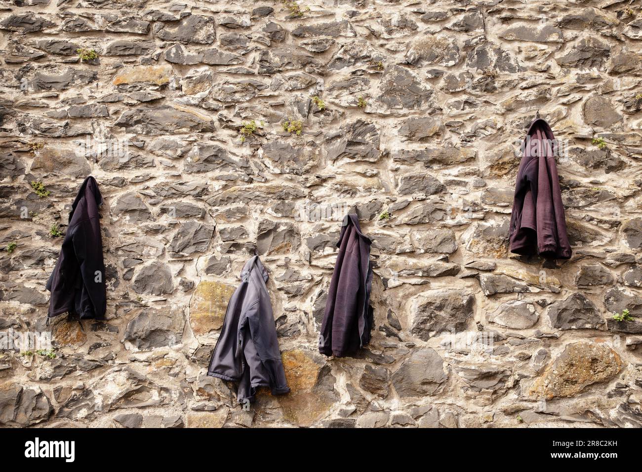 four coats hanging on a wall outside in the street Stock Photo - Alamy