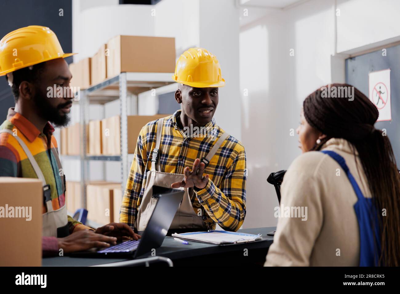 Warehouse workers getting inventory management instruction from supervisor at reception desk ...