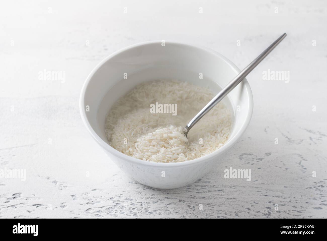 White bowl with long grain rice soaked in water on a light gray ...
