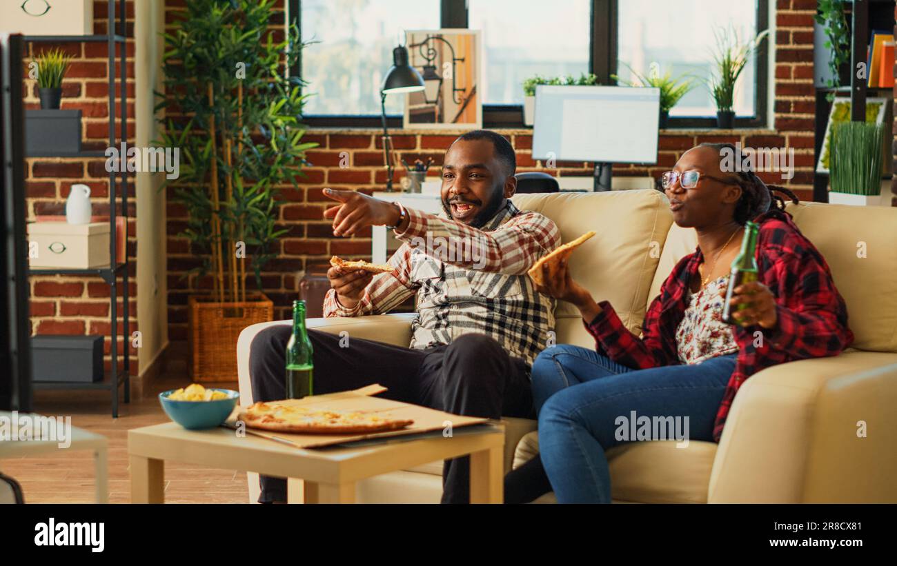 Happy couple eating slices of pizza at television, feeling relaxed ...