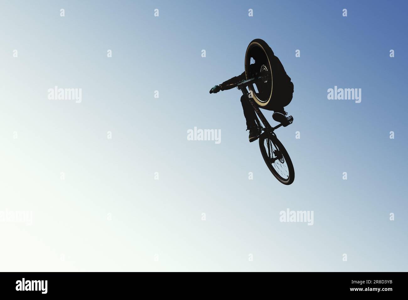 A cyclist mid-jump, in silhouette against the open sky. The image ...