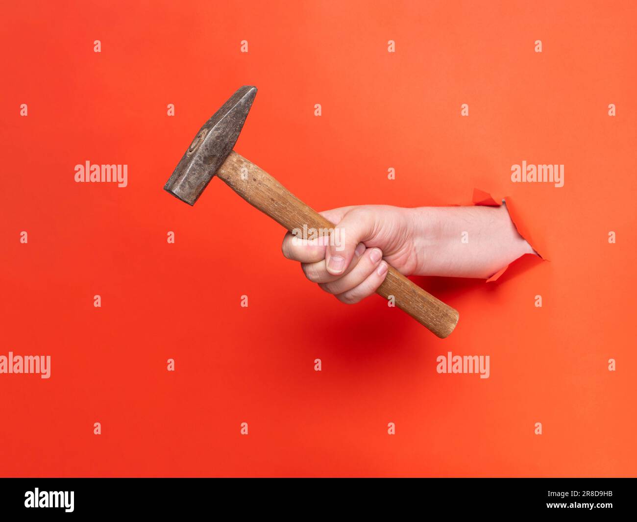 A man's hand holds a hammer through torn orange paper. Concept, hand ...