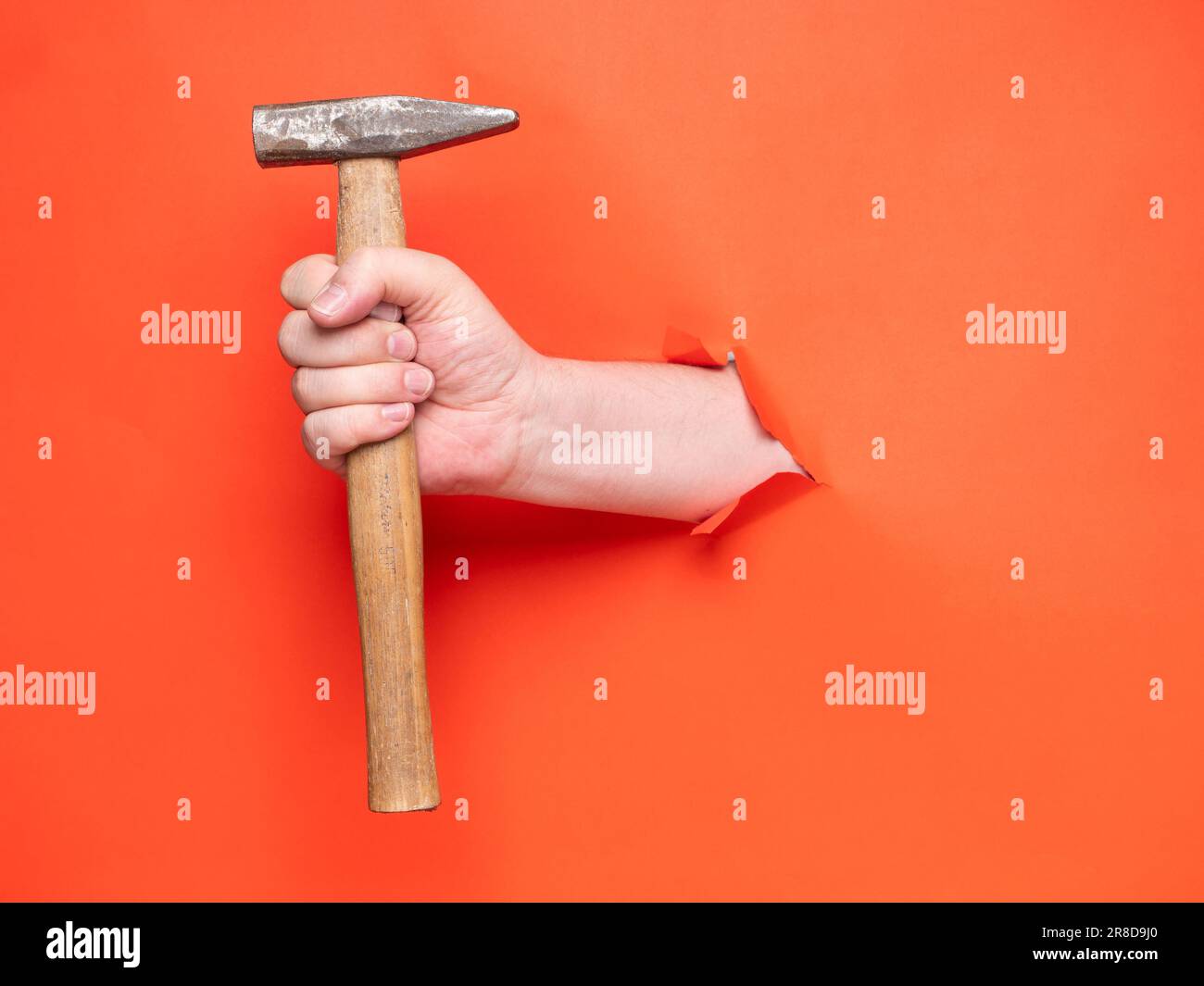 A man's hand holds a hammer through torn orange paper. Concept, hand ...