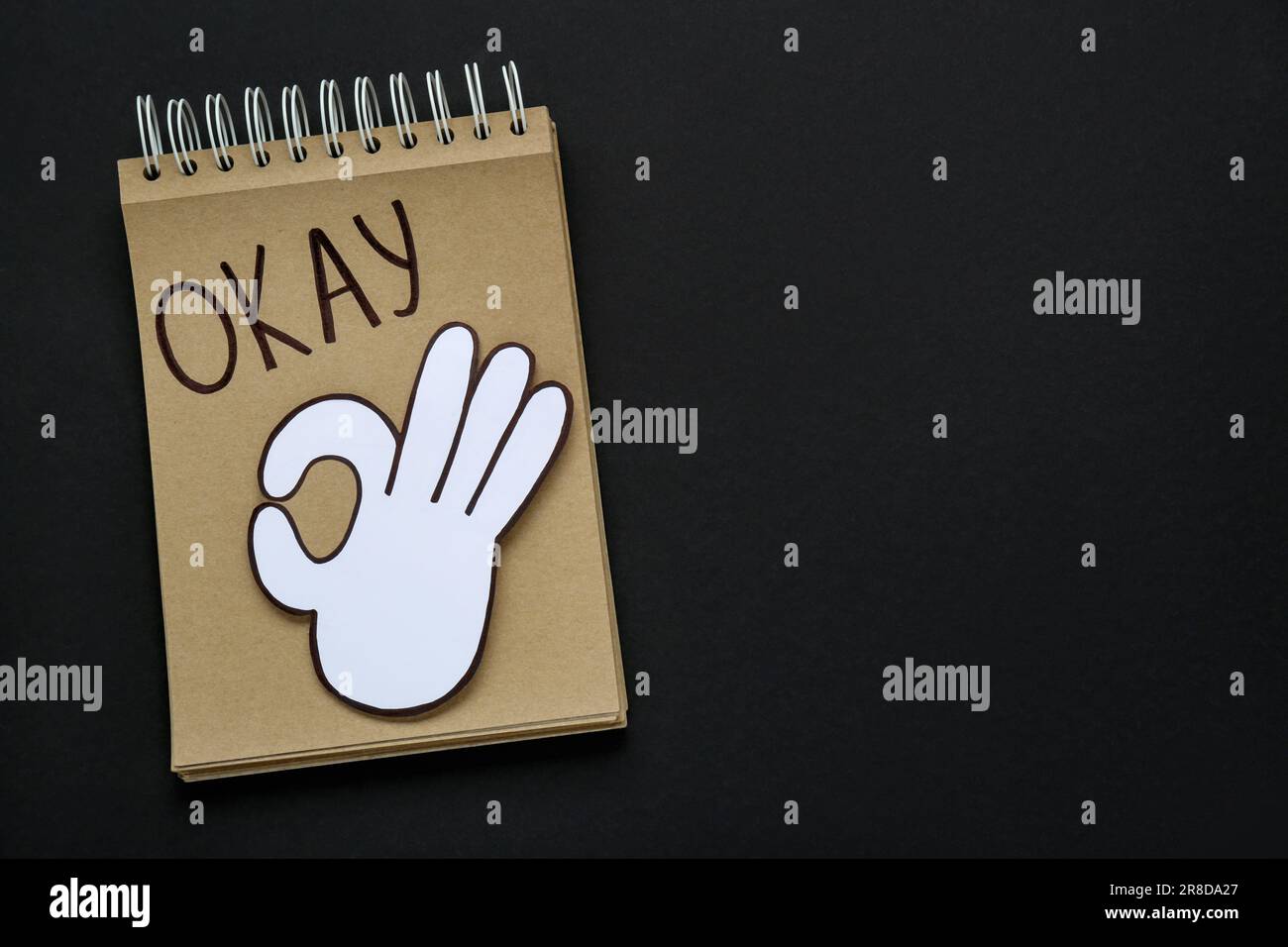 Notepad with word Okay and paper cutout of hand (OK gesture) on black ...