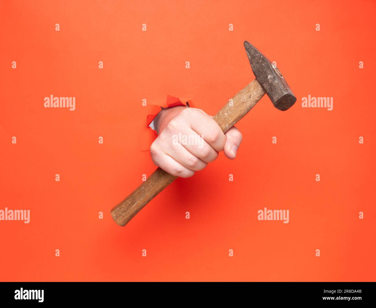 A man's hand holds a hammer through torn orange paper. Concept, hand ...