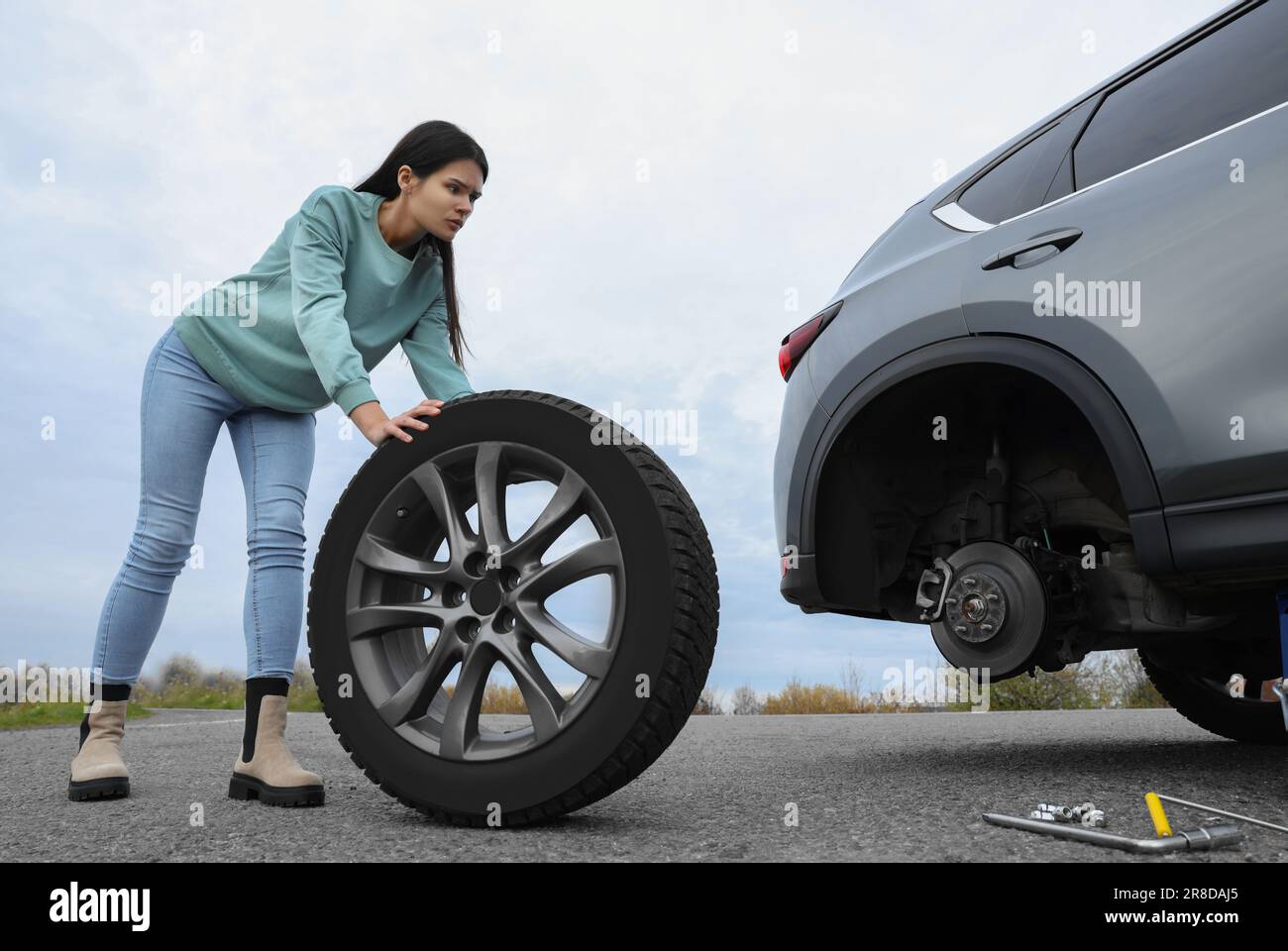Young woman changing tire of car on roadside Stock Photo - Alamy