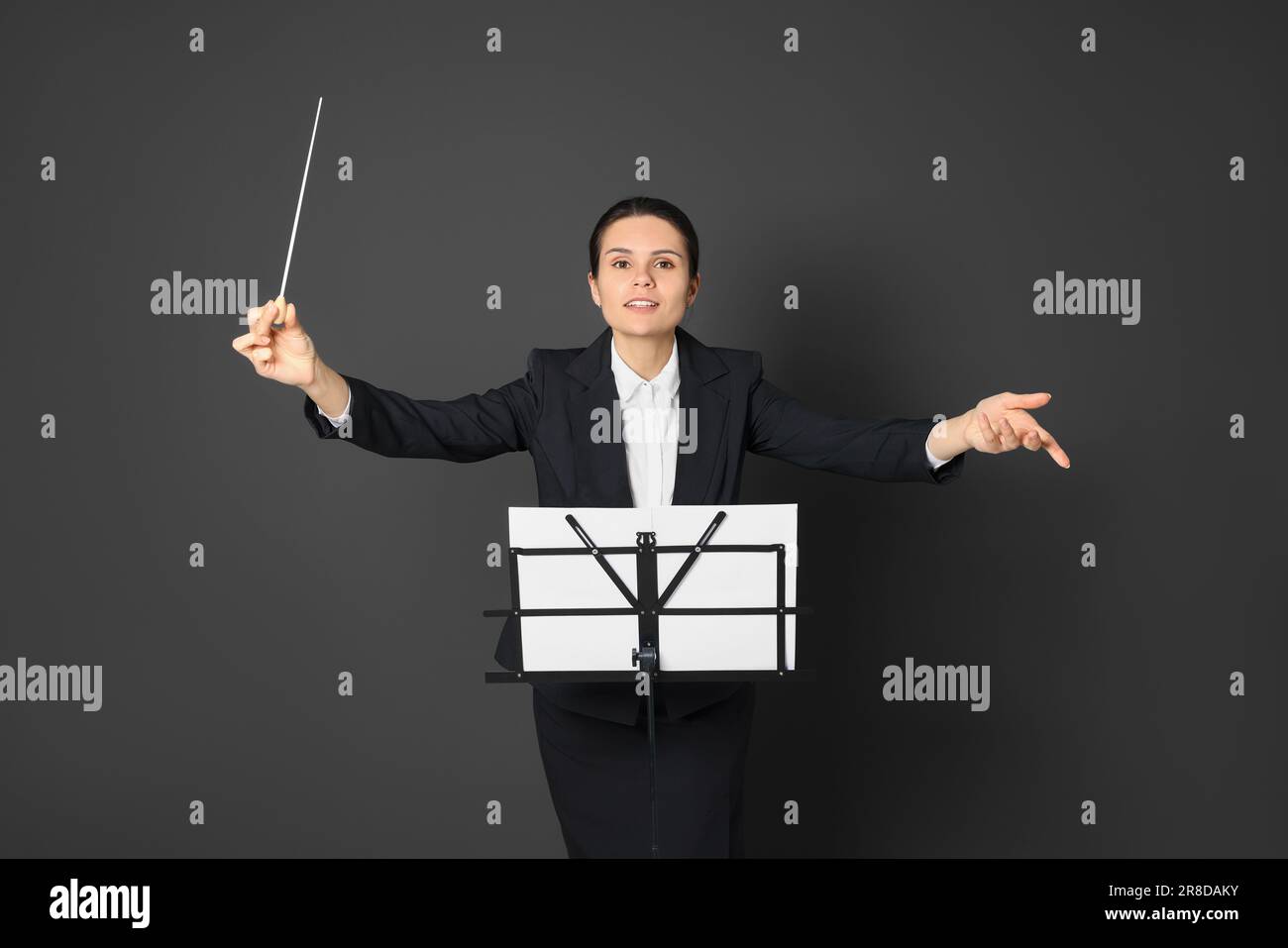 Happy professional conductor with baton and note stand on grey ...
