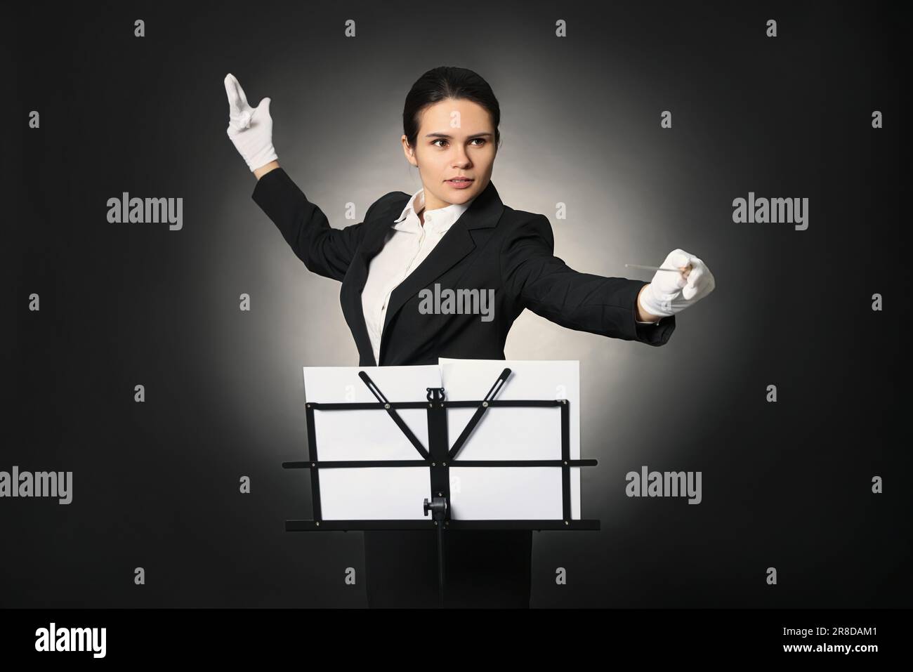 Professional conductor with baton and note stand on black background ...