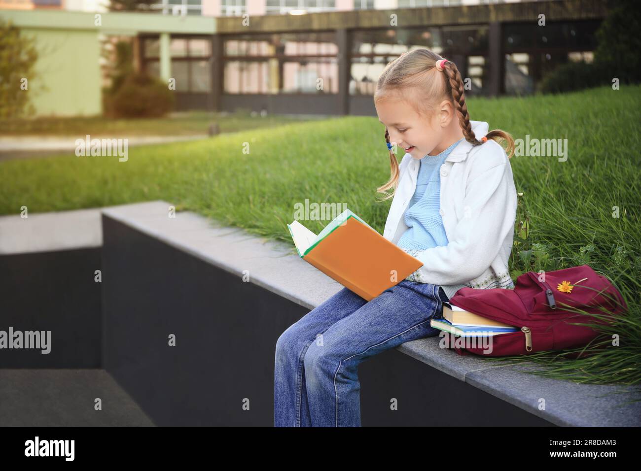 Cute little girl with backpack reading textbook on city street. Space ...