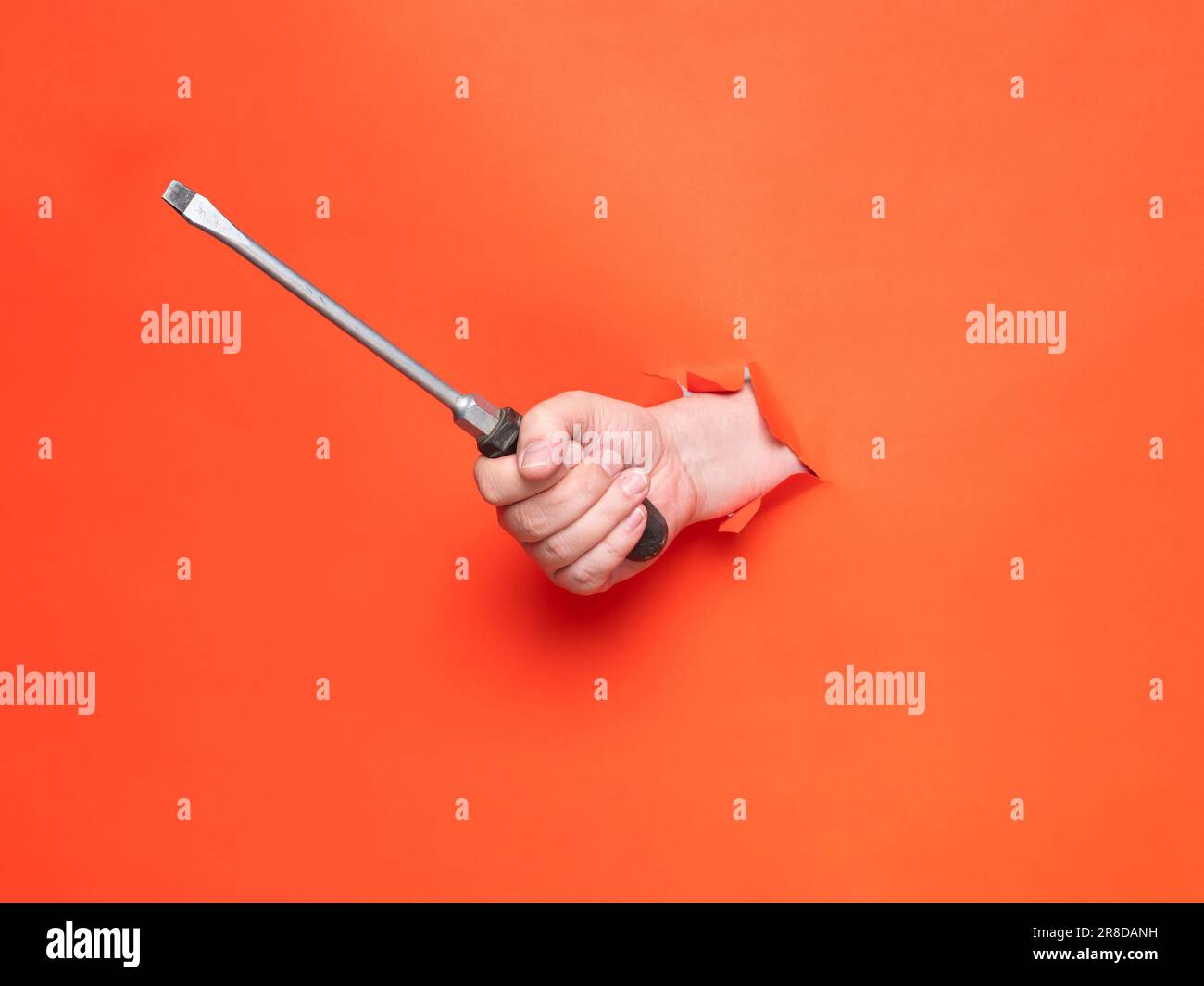 Hand holding a big screwdriver through torn orange paper. No face ...