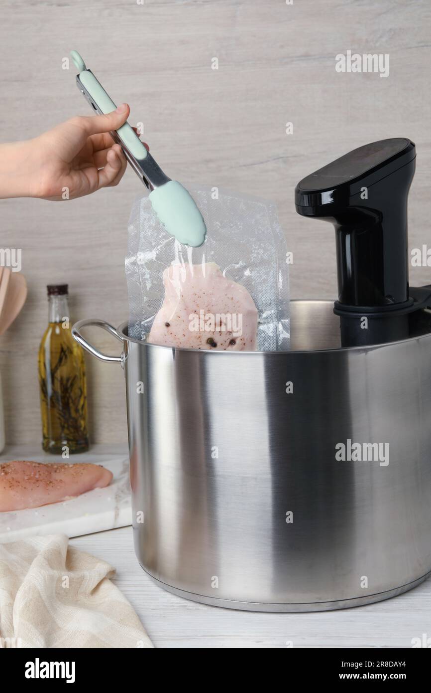 Woman putting vacuum packed meat into pot with sous vide cooker at ...