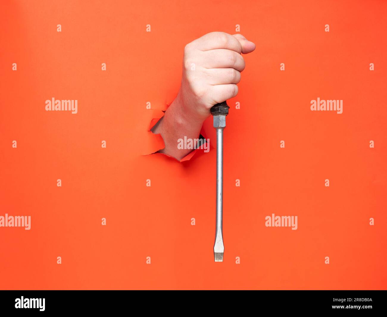 Hand holding a big screwdriver through torn orange paper. No face ...