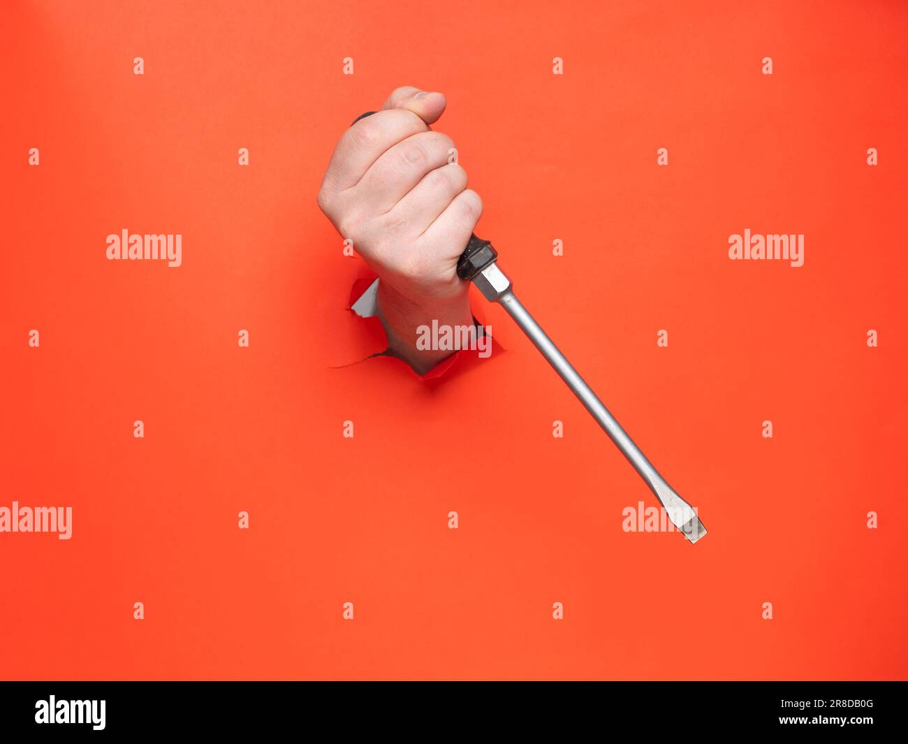 Hand holding a big screwdriver through torn orange paper. No face ...