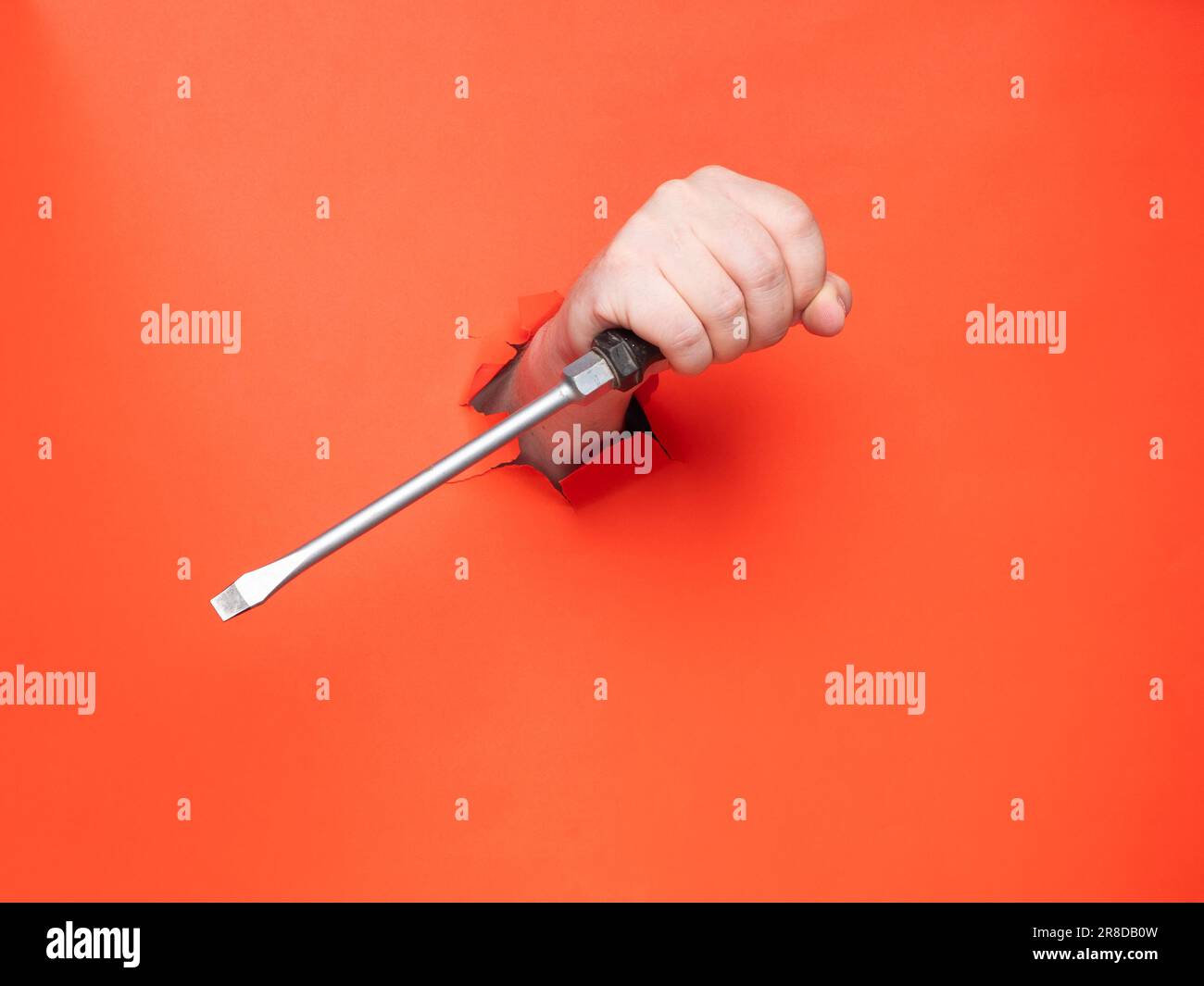 Hand holding a big screwdriver through torn orange paper. No face ...