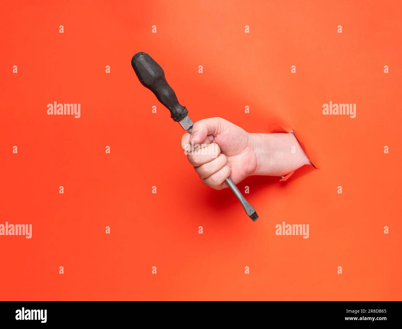 Hand holding a big screwdriver through torn orange paper. No face ...