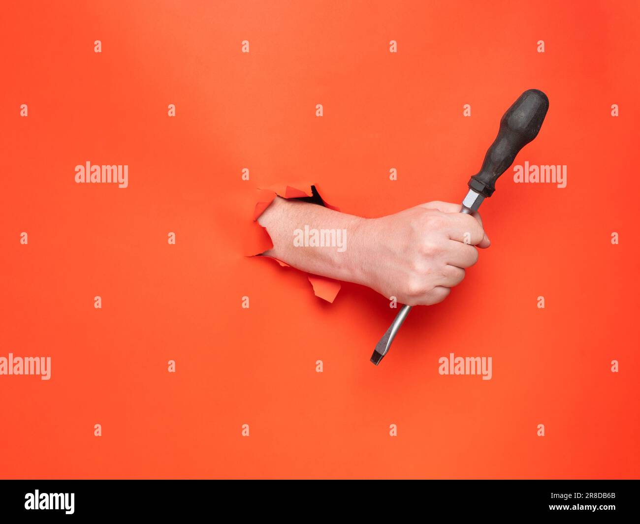 Hand holding a big screwdriver through torn orange paper. No face ...
