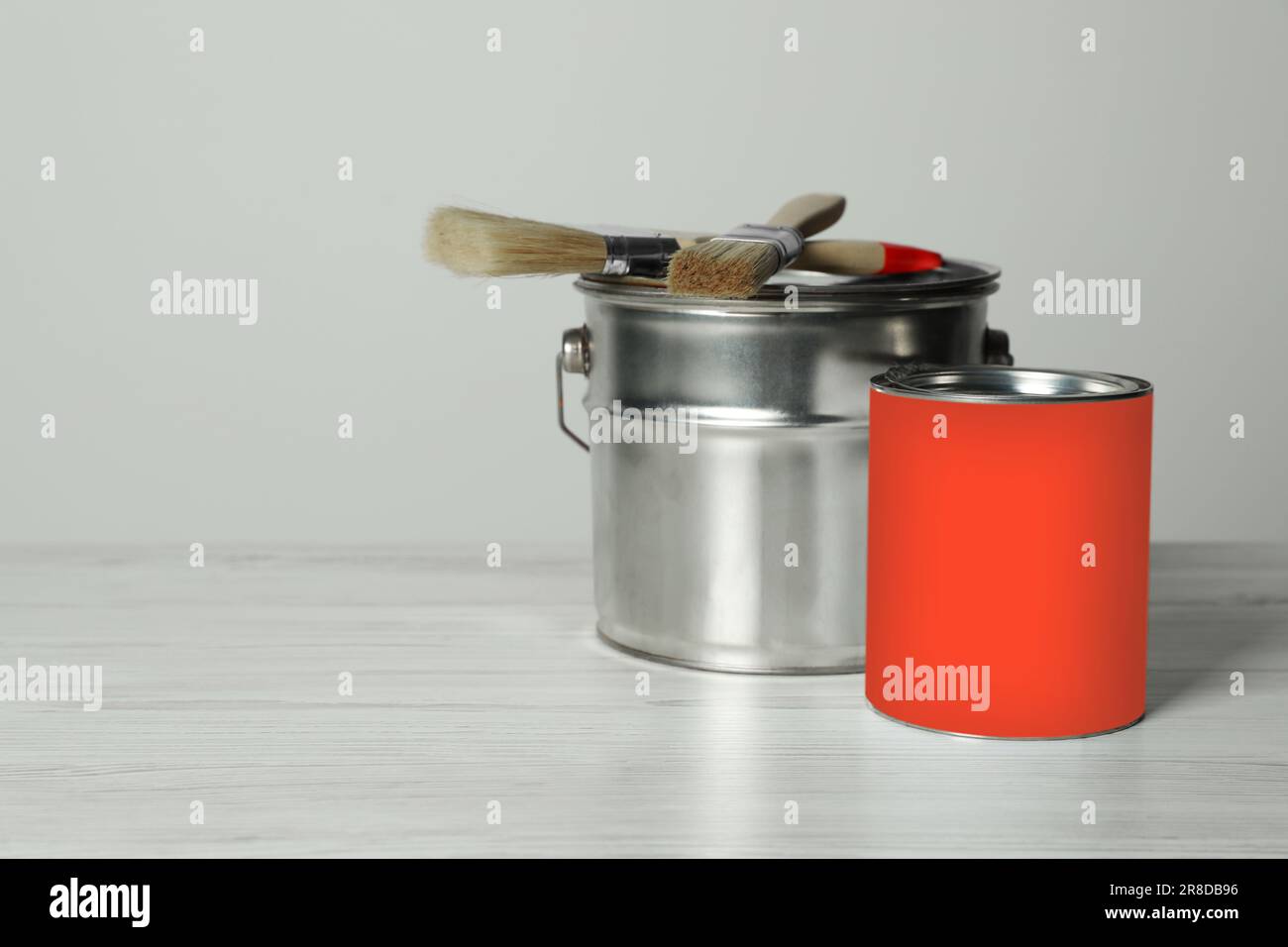 Can of orange paint, bucket and brushes on white wooden table. Space ...