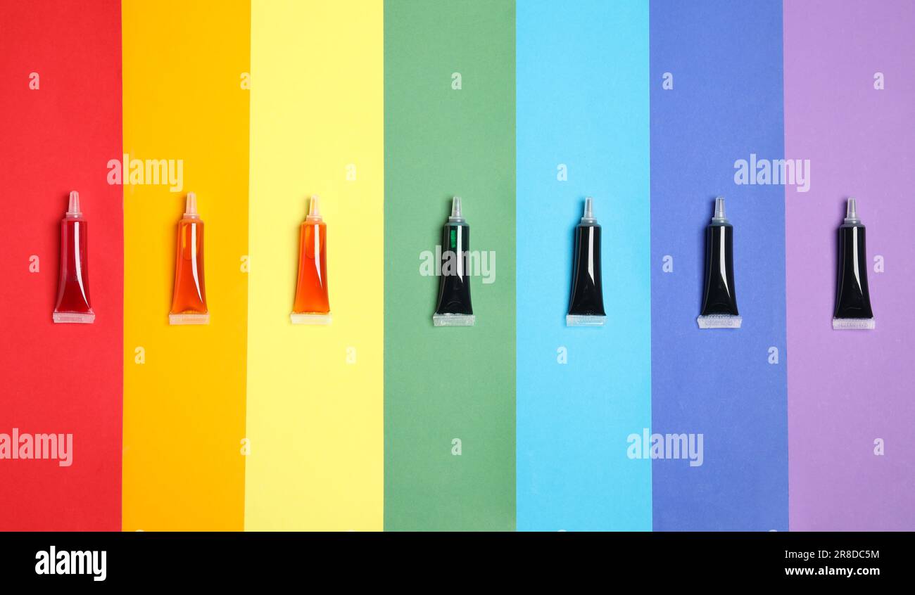 Tubes with different food coloring on rainbow background, flat lay ...