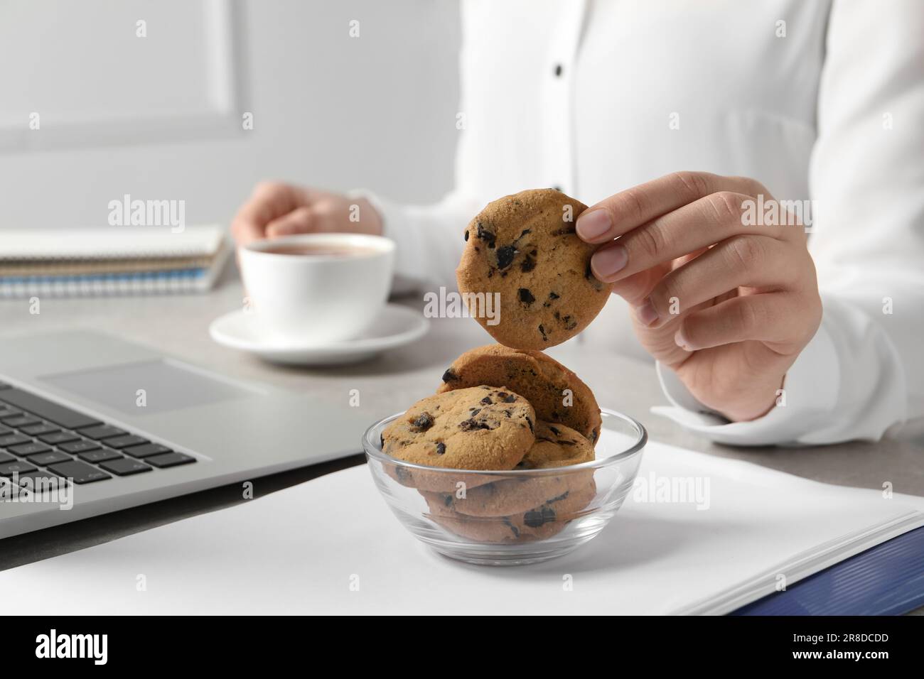Woman taking chocolate chip cookie from bowl while drinking tea in ...