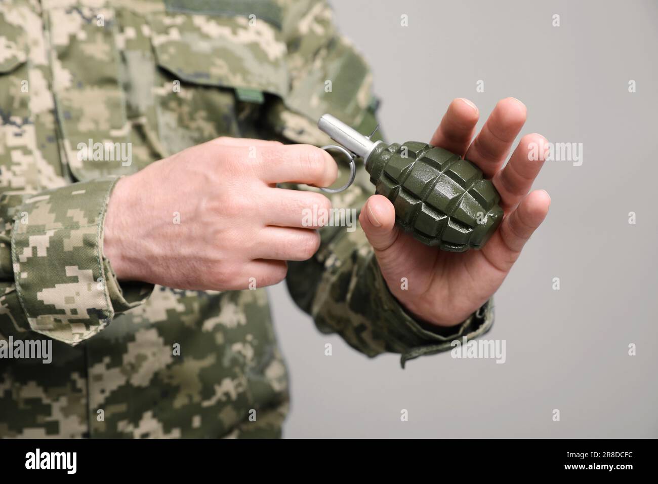 Soldier pulling safety pin out of hand grenade on light grey background ...
