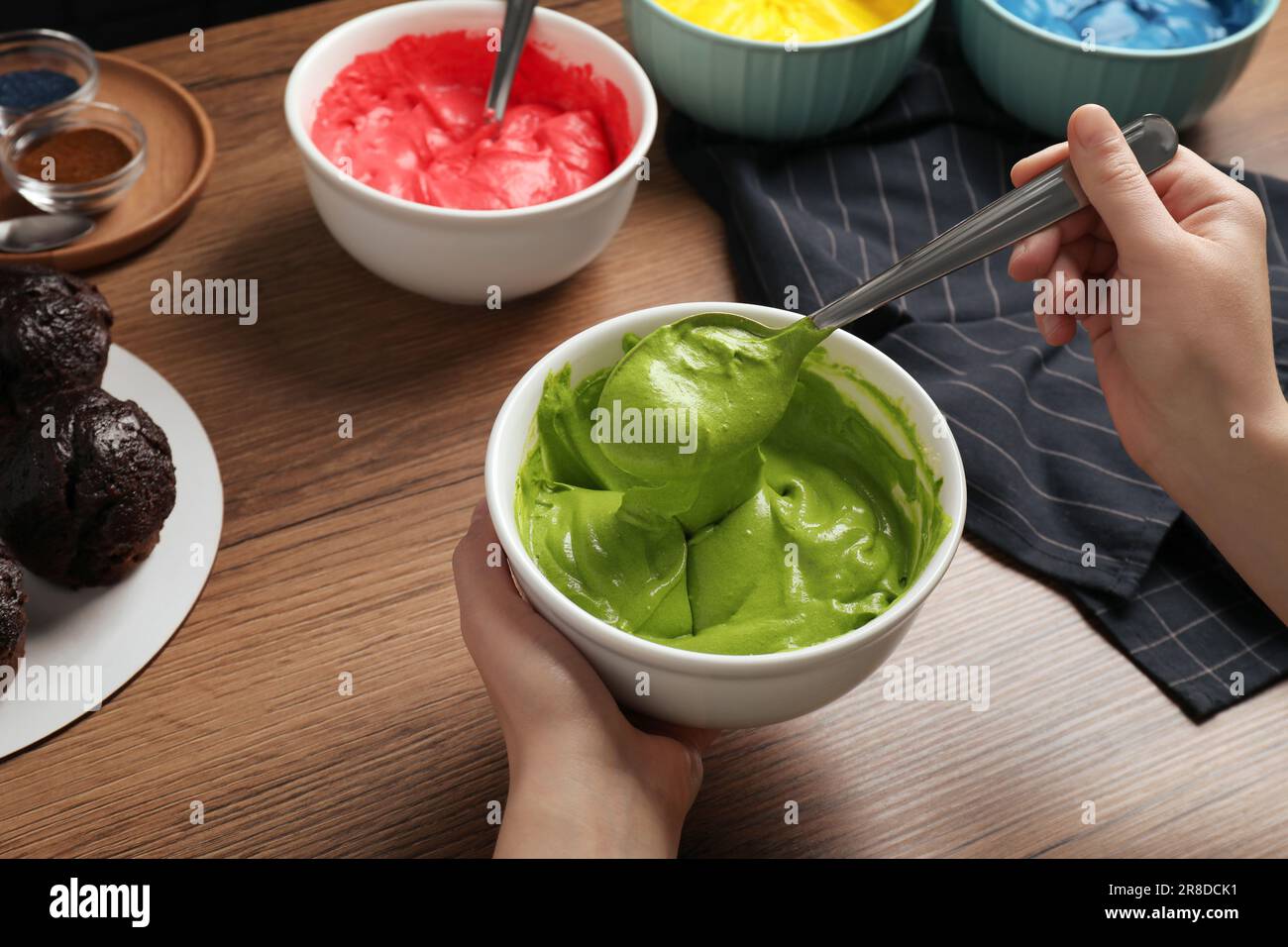 Woman mixing cream with green food coloring at wooden table, closeup ...