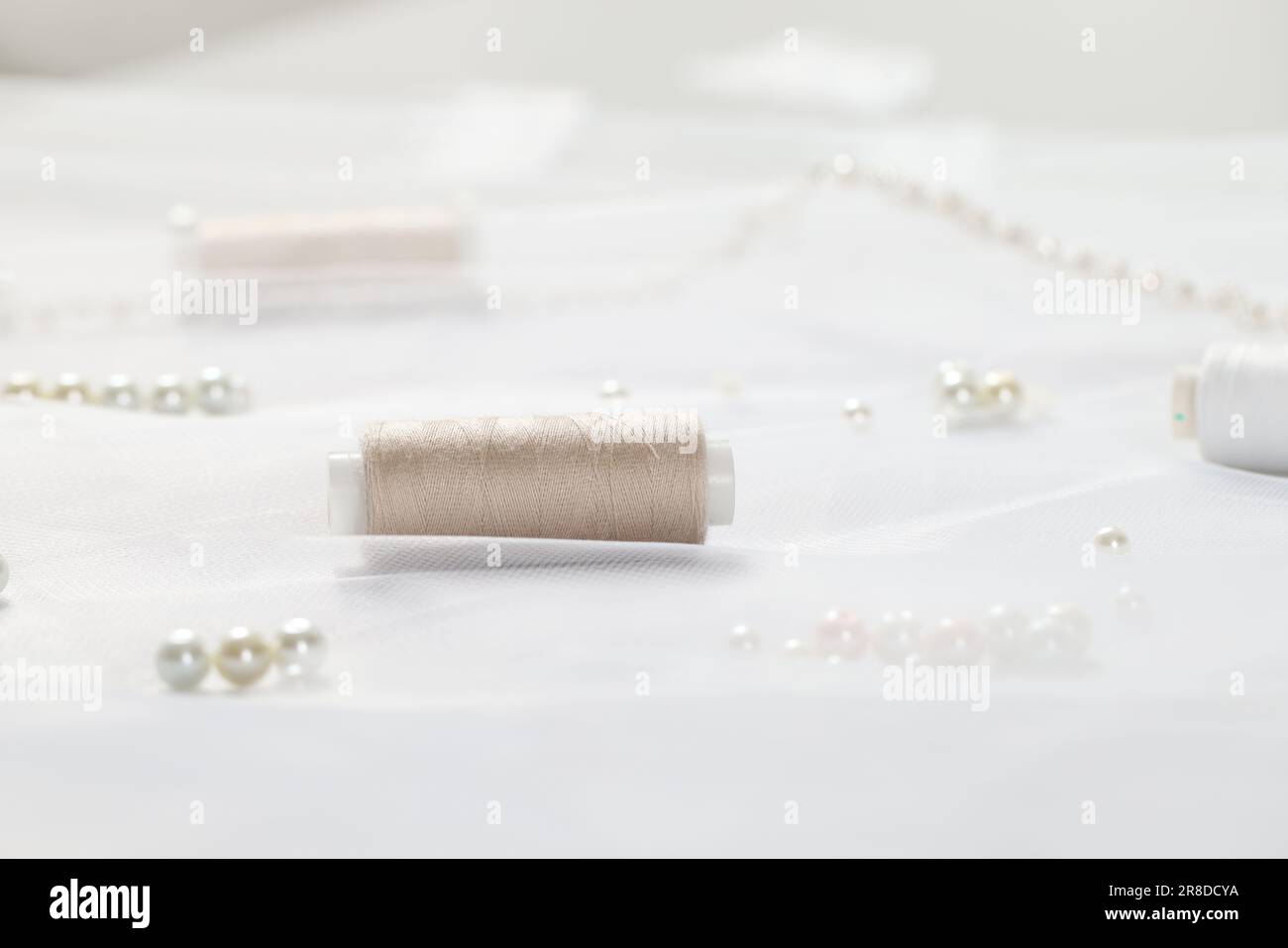 Spool of thread and beads on white fabric, closeup Stock Photo - Alamy