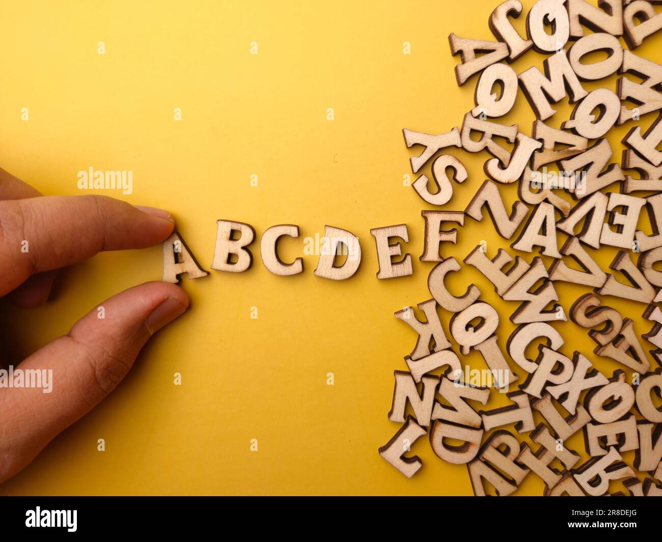 A person's hand is arranging wooden letters in the order of ABCDE on a ...