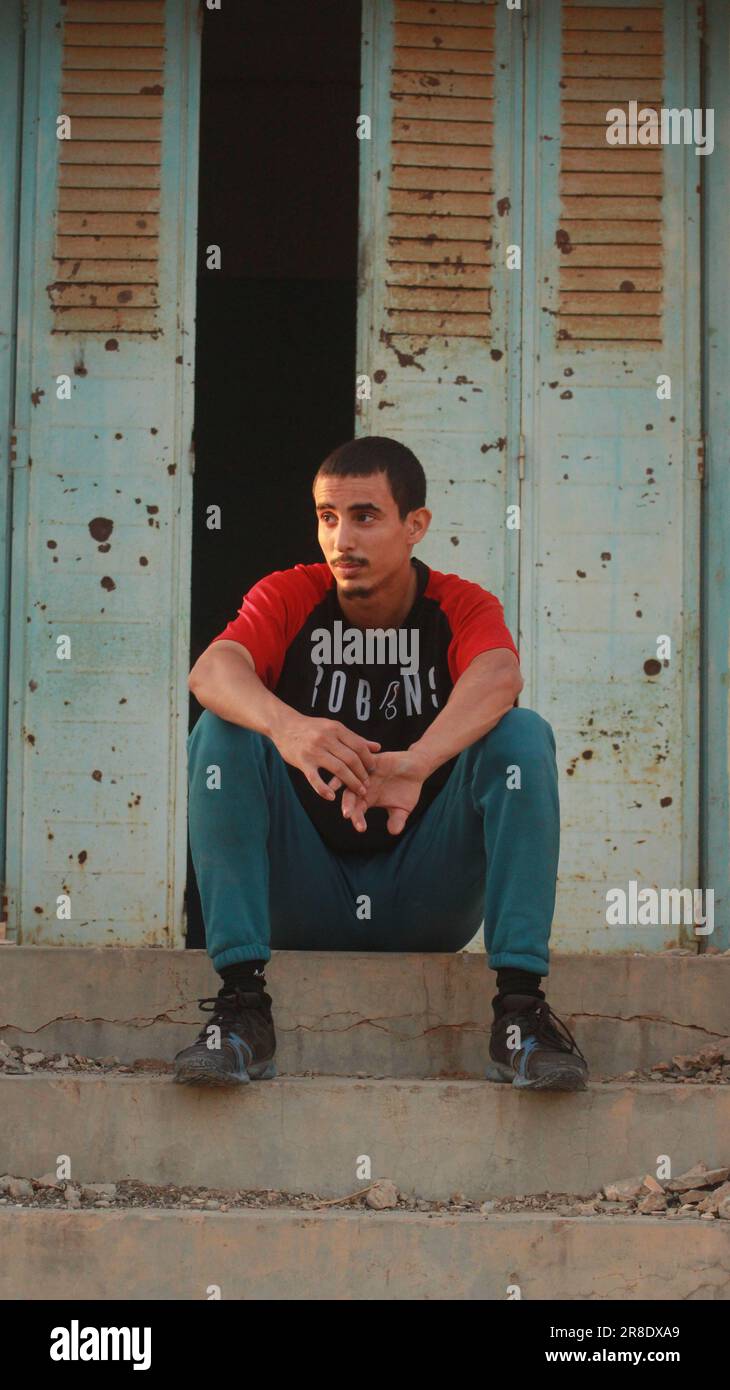 Young man sitting in front of a gate Stock Photo - Alamy