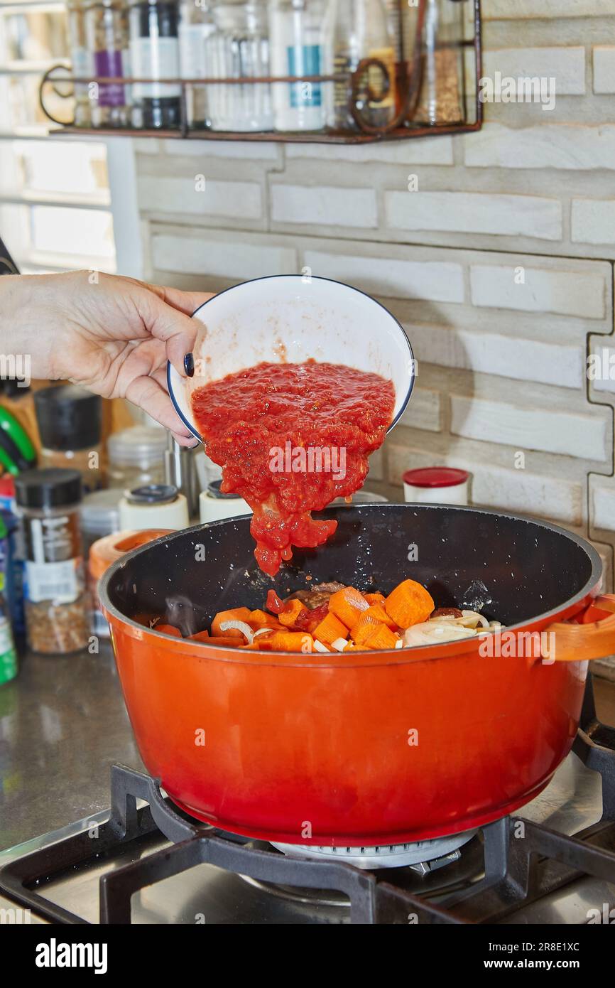 Chef adds tomato paste to the pot of ingredients on the gas stove Stock ...