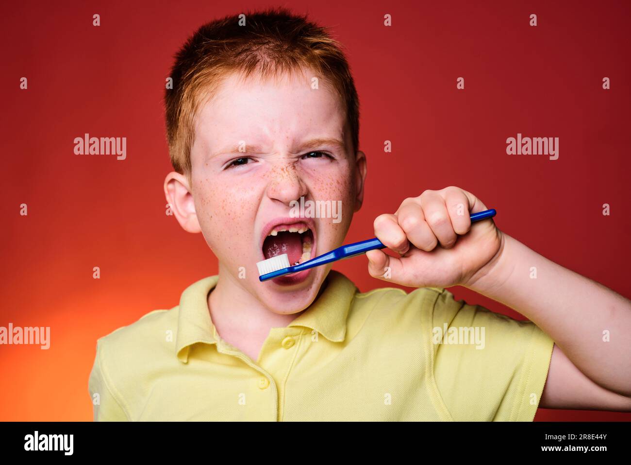 Smiley boy without one teeth with toothbrush isolated on red background ...