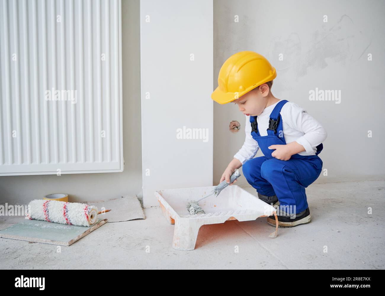 Little boy construction worker crouching down and preparing paint ...