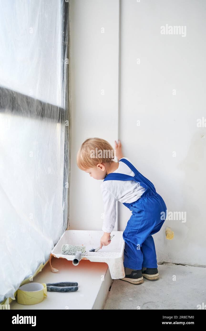 Little boy construction worker standing by the window and painting ...