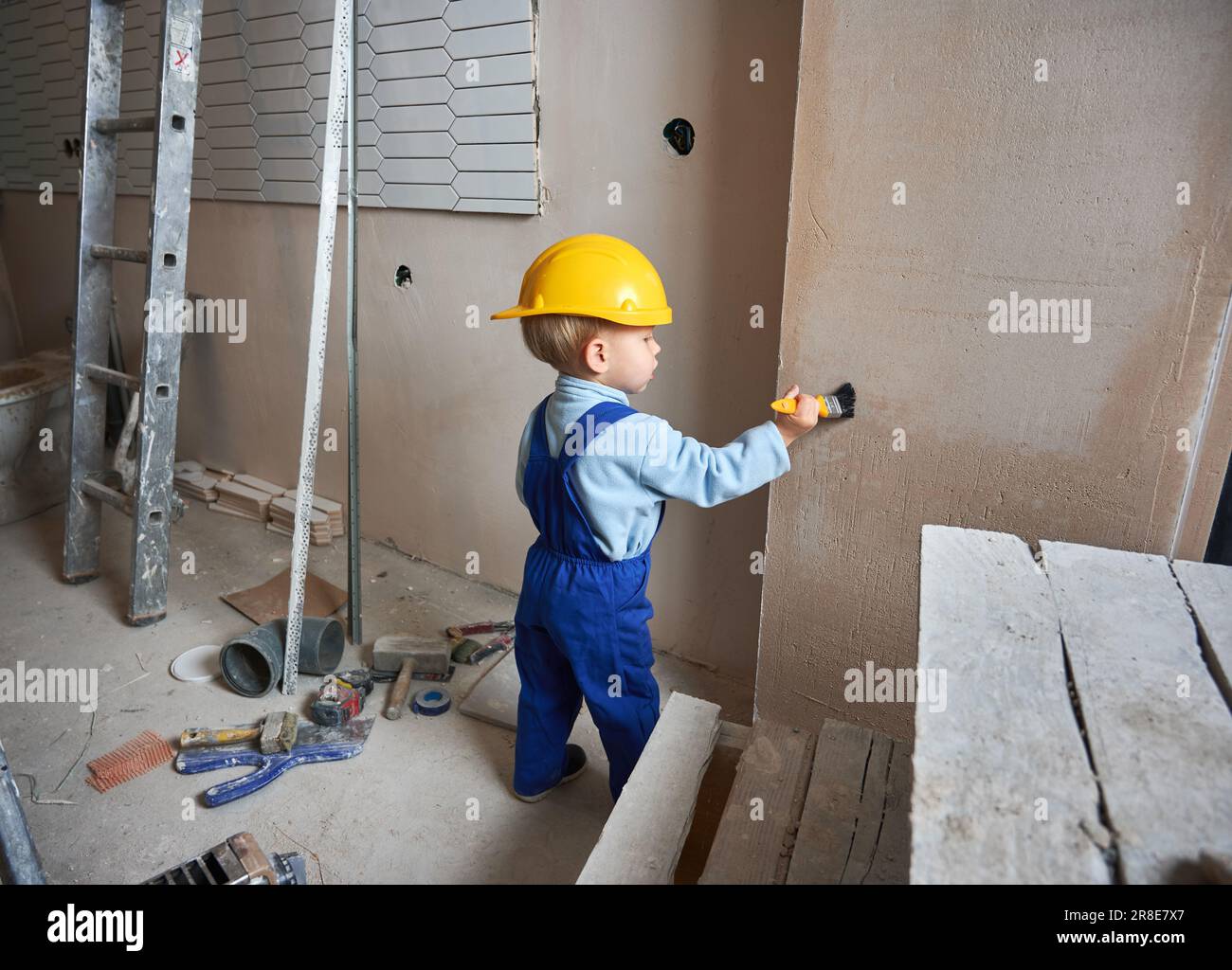 Full length of child construction worker painting wall with brush in ...