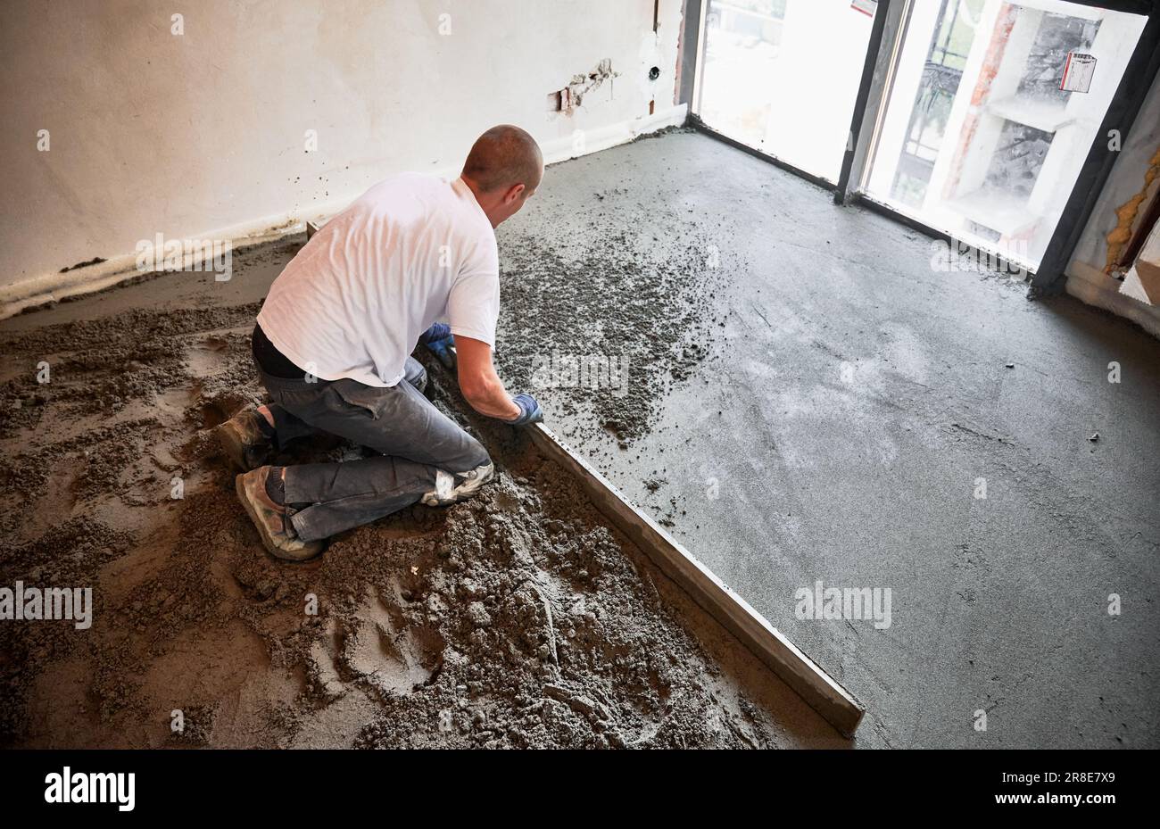 Male construction worker using screed rail while screeding floor in ...