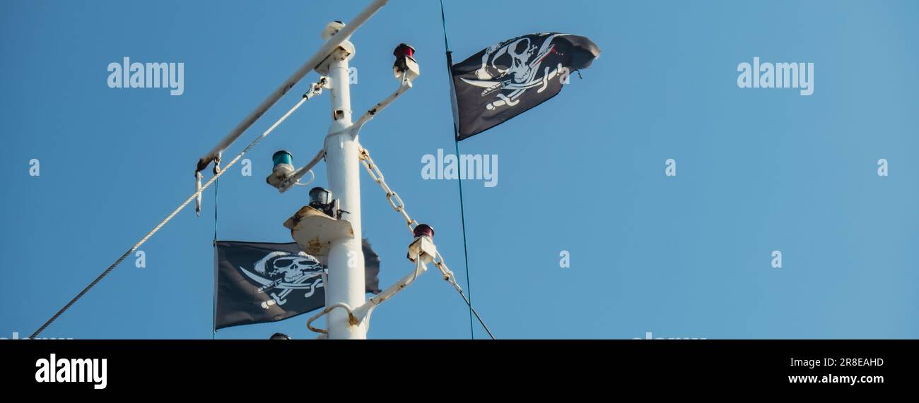 Jolly Roger or pirate ship flag waving with flagpole and blue sky ...