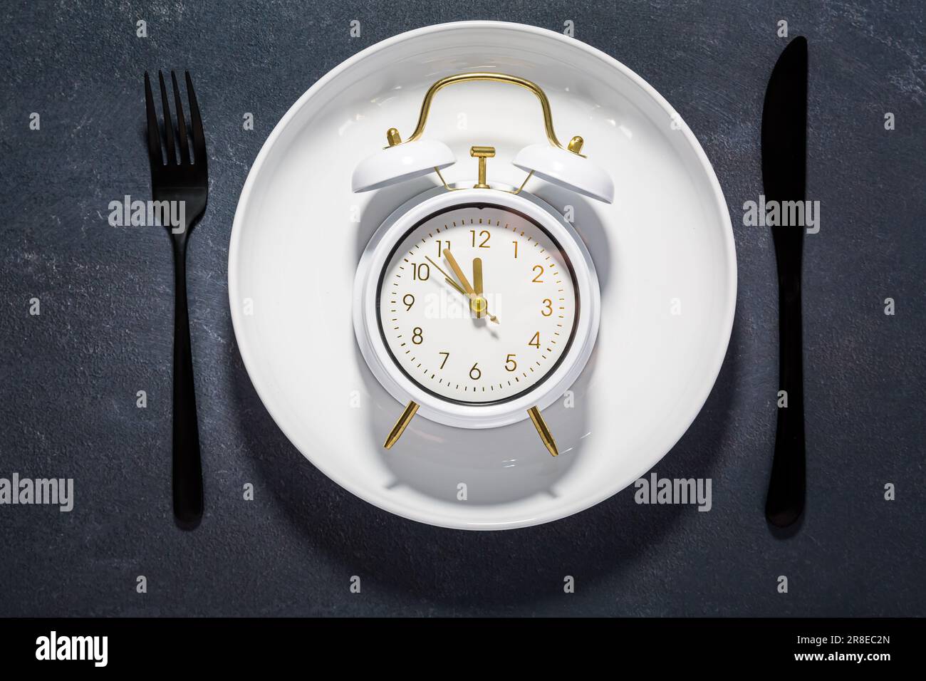 White plate and clock on a dark background with copy space. Concept of ...
