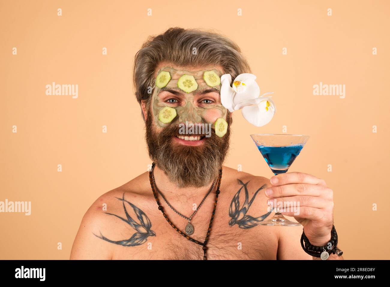 Funny man with clay mask and cucumber slices on face drink cocktail ...