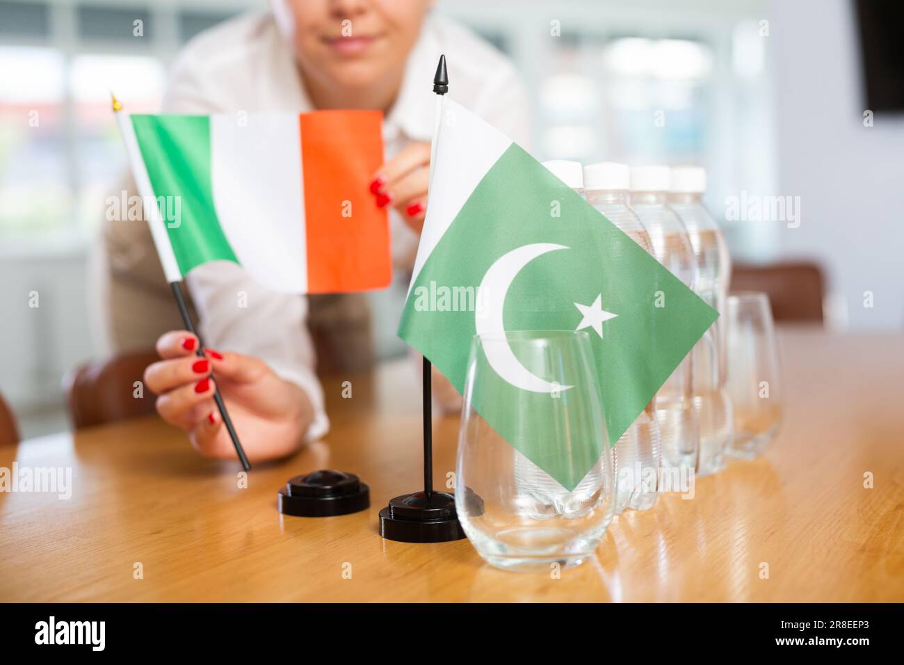 Young woman putting flags of Pakistan and Italy on table in office ...