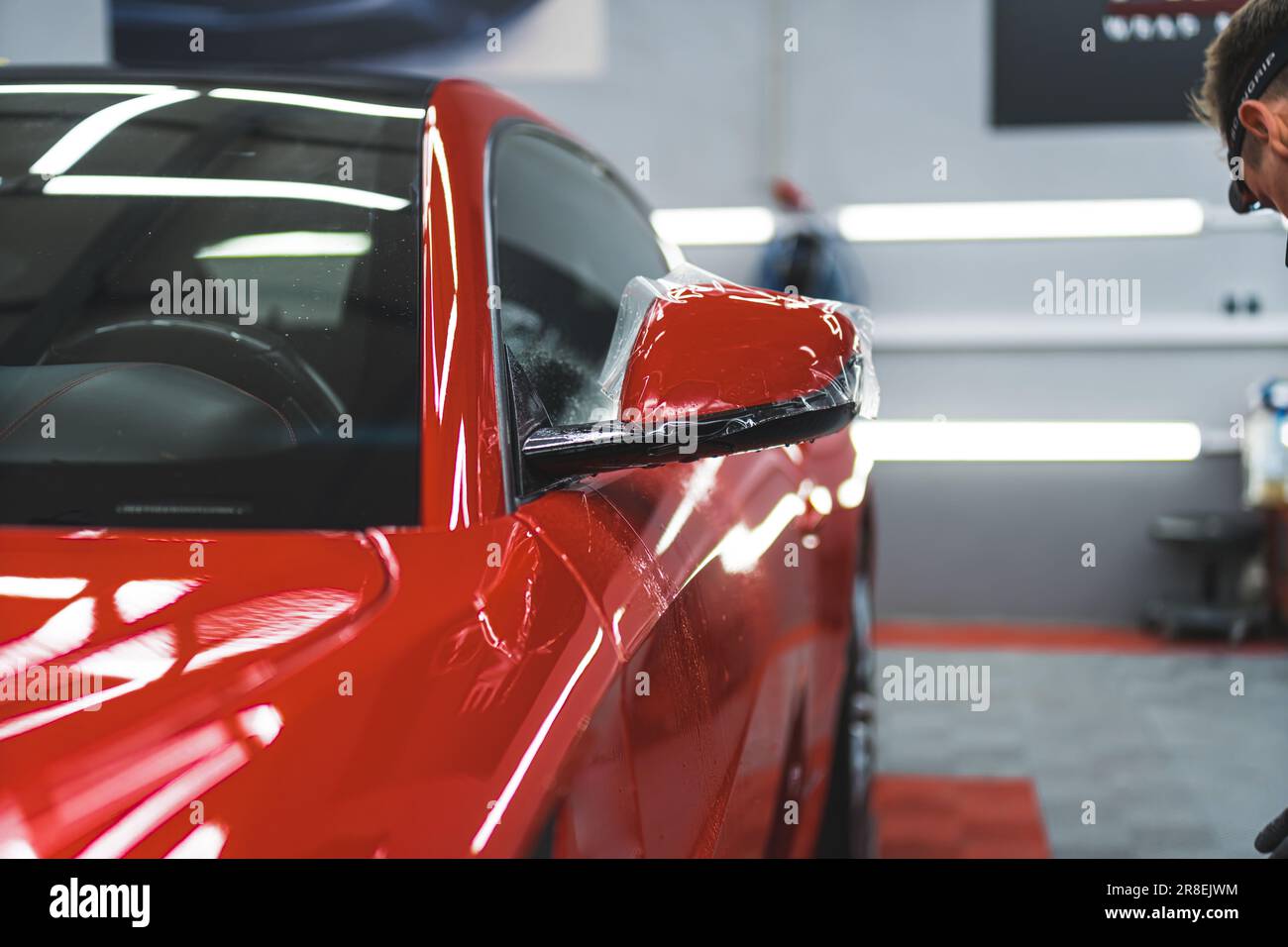 Front view of car detailing process. Specialist using PPF to cover red ...