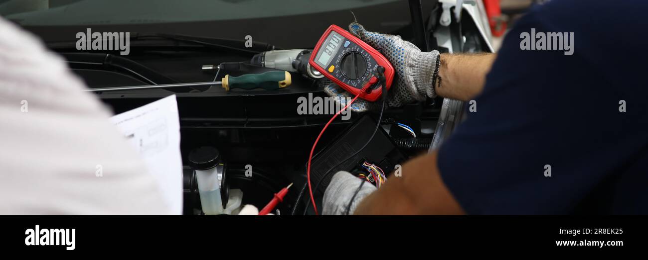 Car repairman checking and testing car battery with digital electronic ...