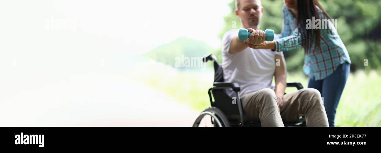 Female physiotherapist helps disabled man in wheelchair to lift weight ...