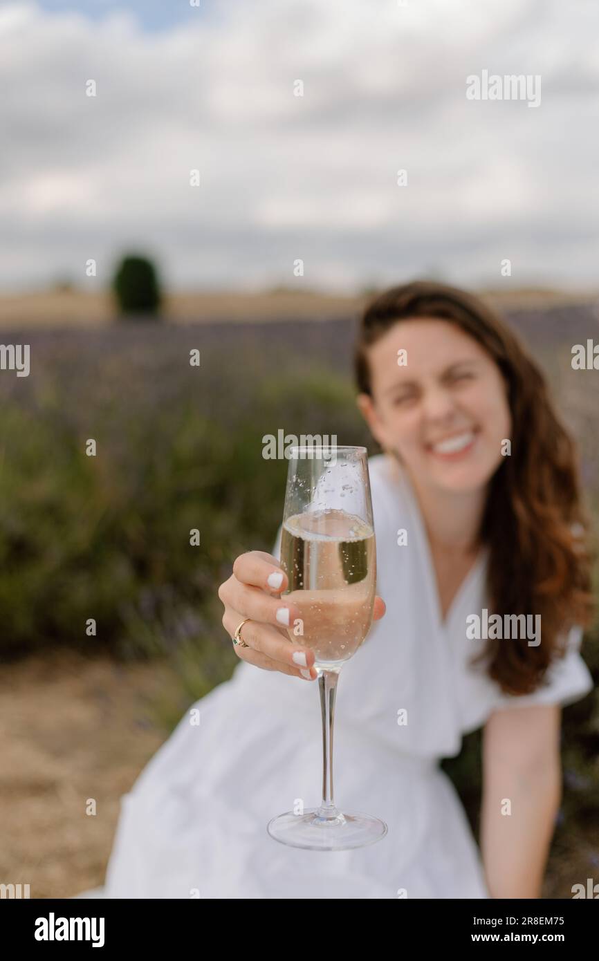 A Caucasian woman in a lavender field, holding a glass of Prosecco in ...