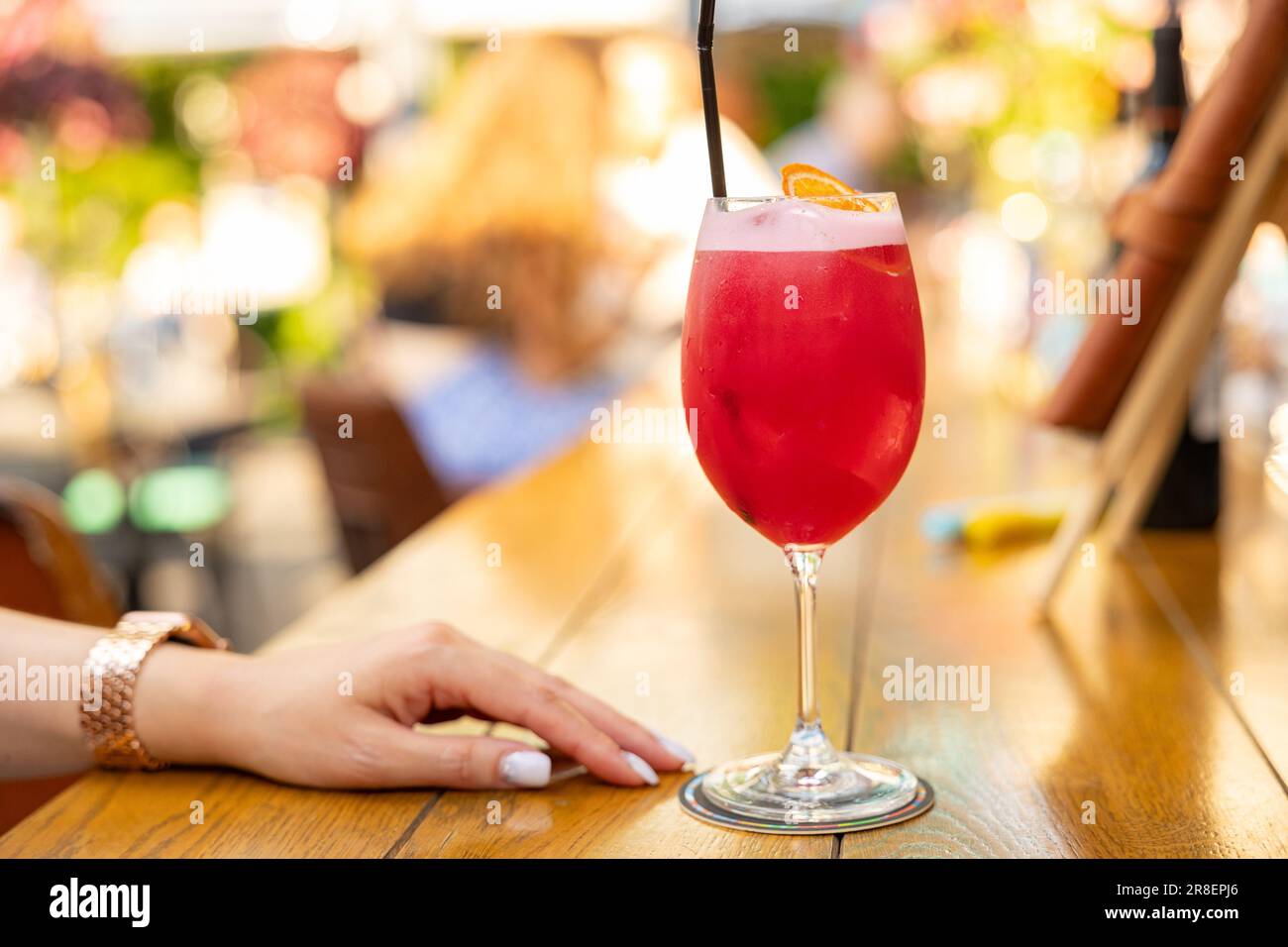 A red cocktail stands on a table in a restaurant next to a woman's hand ...