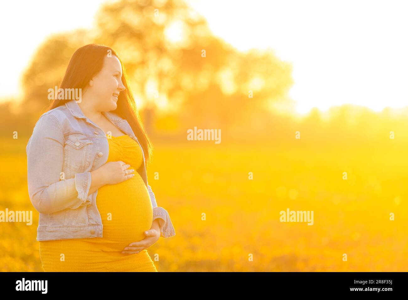 Young pregnant woman smilling to huge belly during lovely summer sunset ...